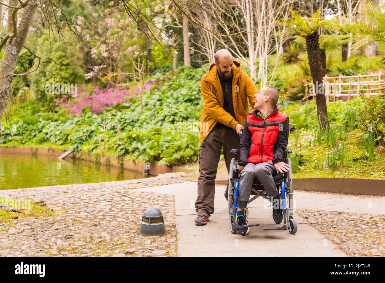 Paralyzed young man in a wheelchair being pushed by a friend in a ...
