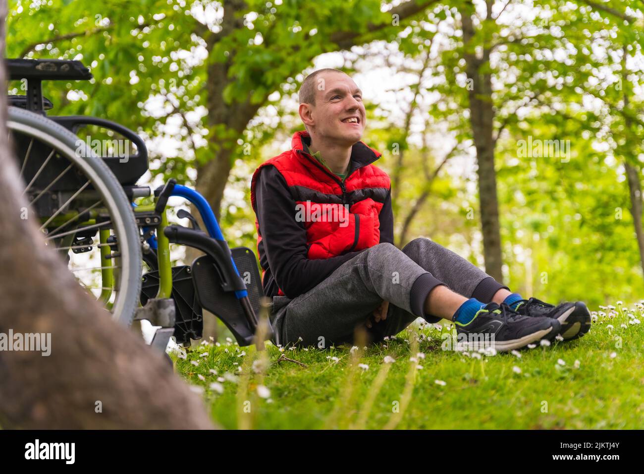 Portrait of a paralyzed young man sitting on the grass next to the ...