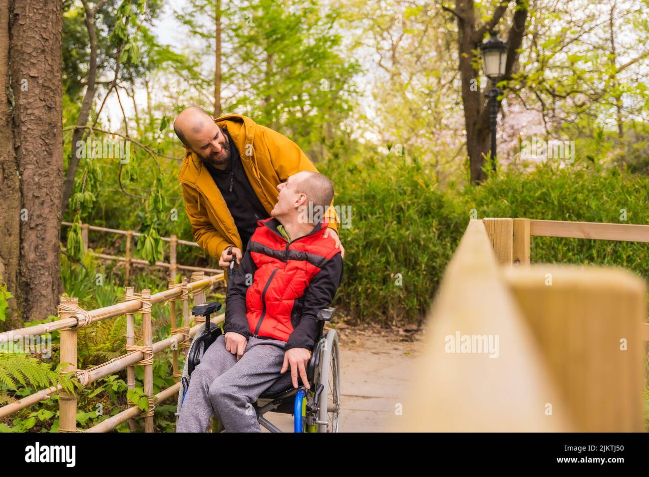 Paralyzed young man in the wheelchair being pushed by a friend in a ...