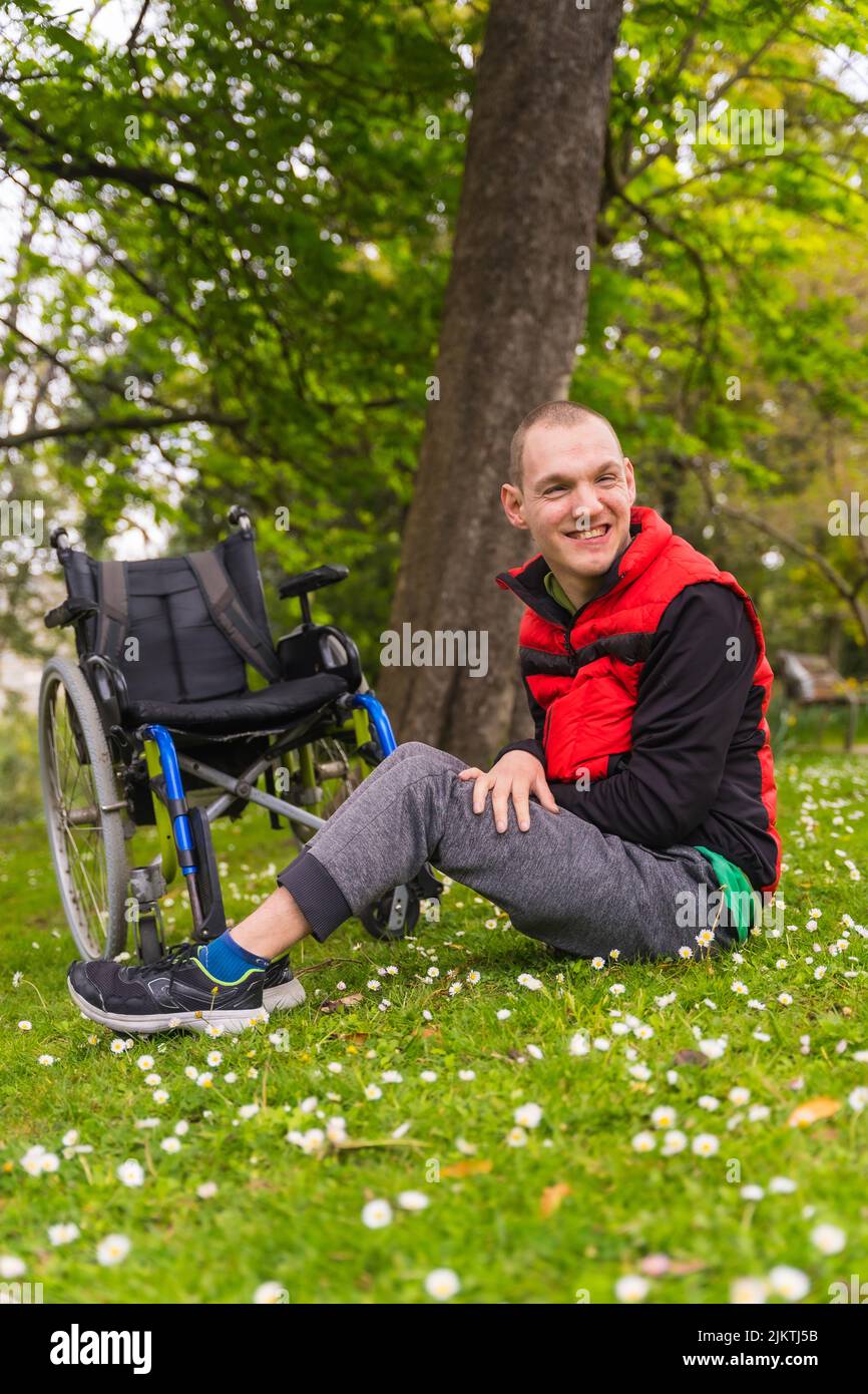 Portrait of a paralyzed young man sitting on the grass next to the ...