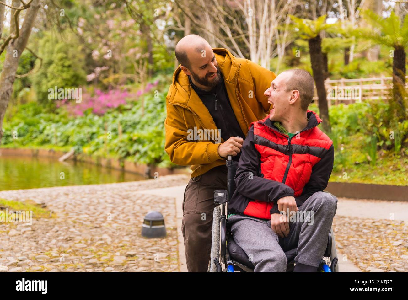 Paralyzed young man in the wheelchair being pushed by a friend in a ...