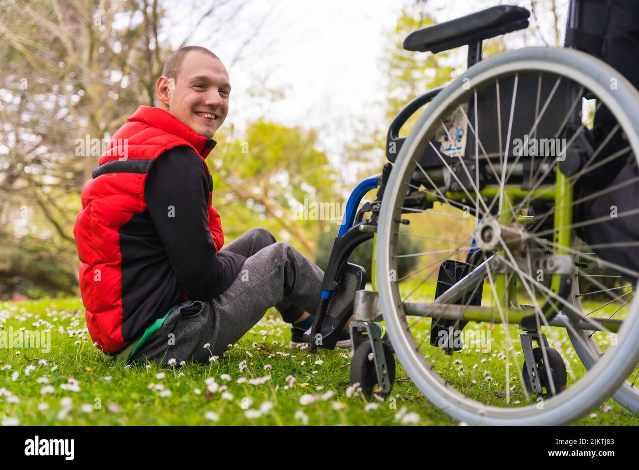 Paralyzed young man sitting on the grass next to the wheelchair next to ...