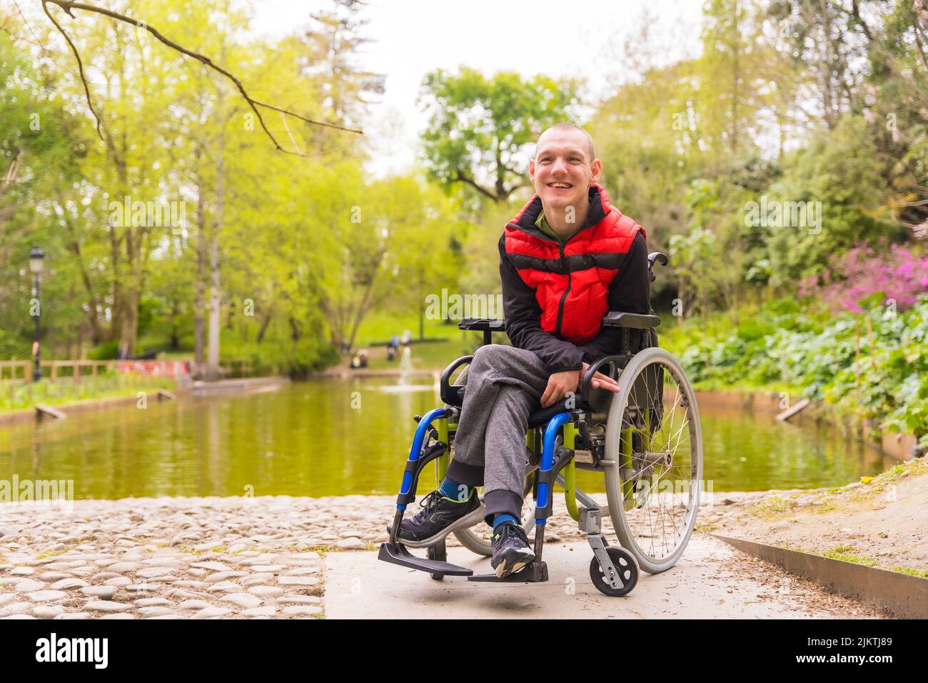 Portrait of a paralyzed young man in a public park in the city. Sitting ...