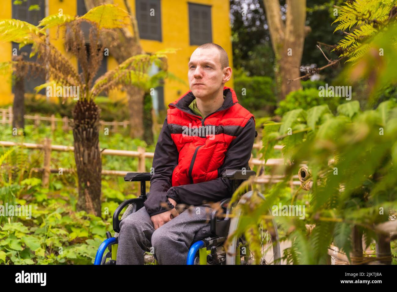 Portrait of a paralyzed young man in a red vest in a public park in the ...