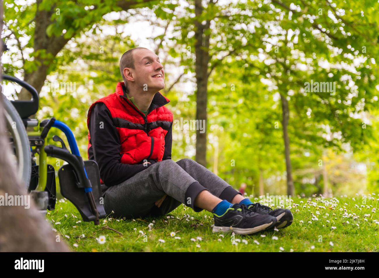 Portrait of a paralyzed young man sitting on the grass next to the ...