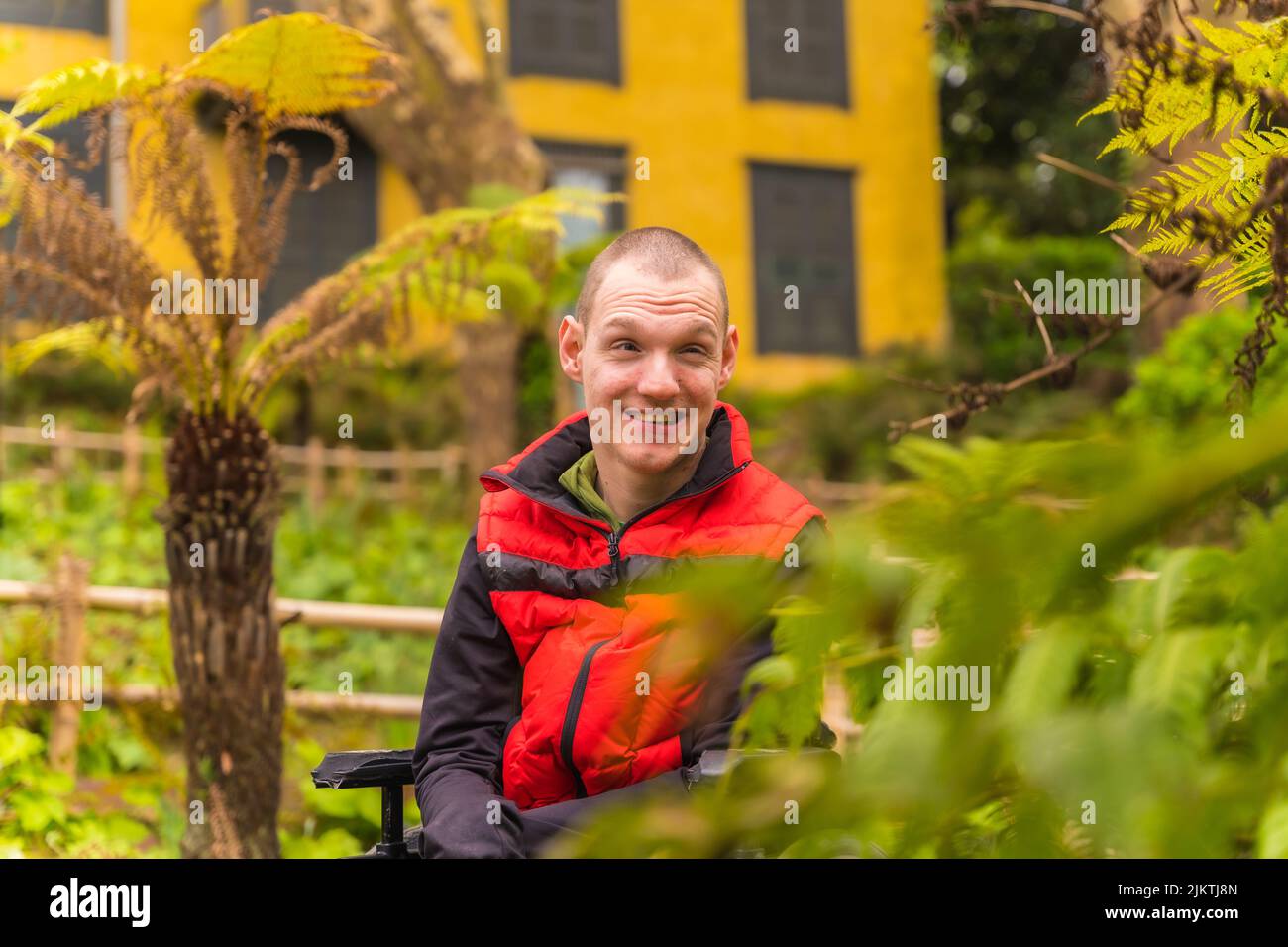 Portrait of a paralyzed young man in a public park in the city. Sitting ...