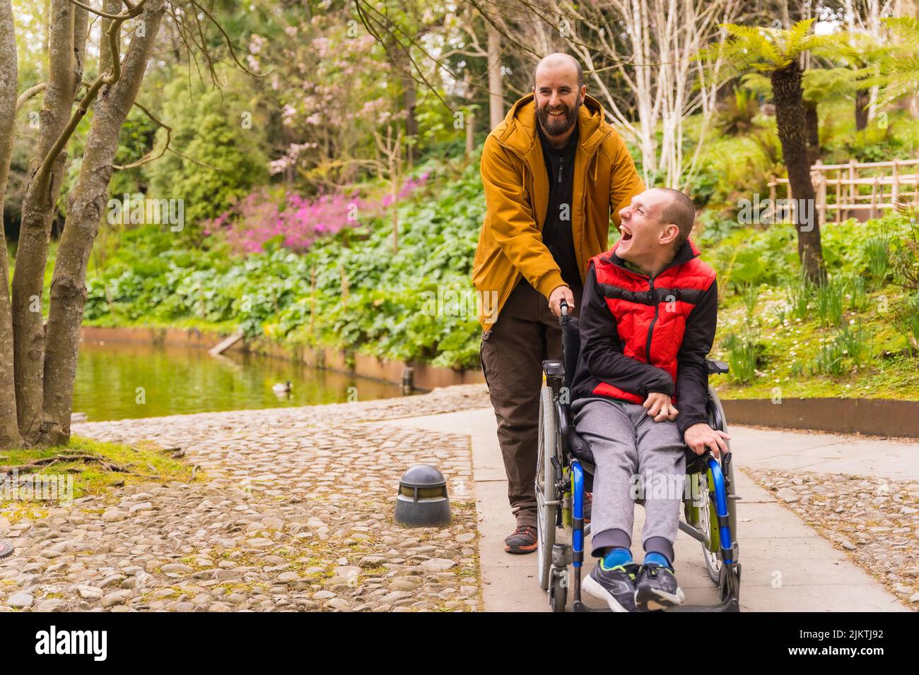 Paralyzed young man in a wheelchair being pushed by a friend in a ...