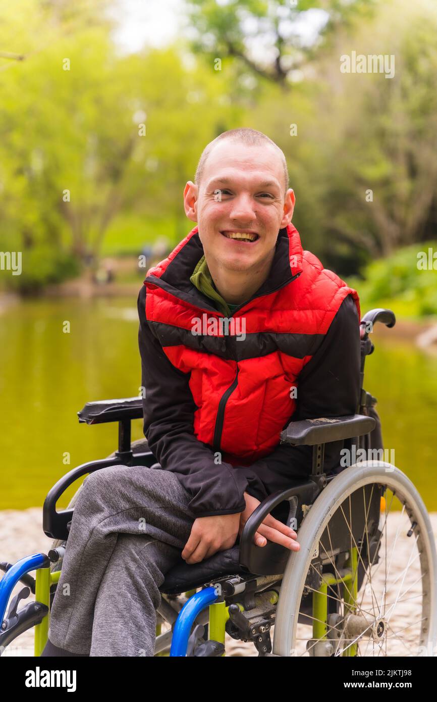 Portrait of a paralyzed young man in a public park in the city. Sitting ...