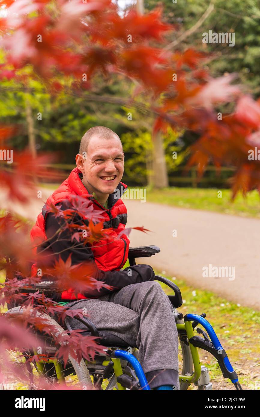 Portrait of a paralyzed young man in a red vest in a public park in the ...