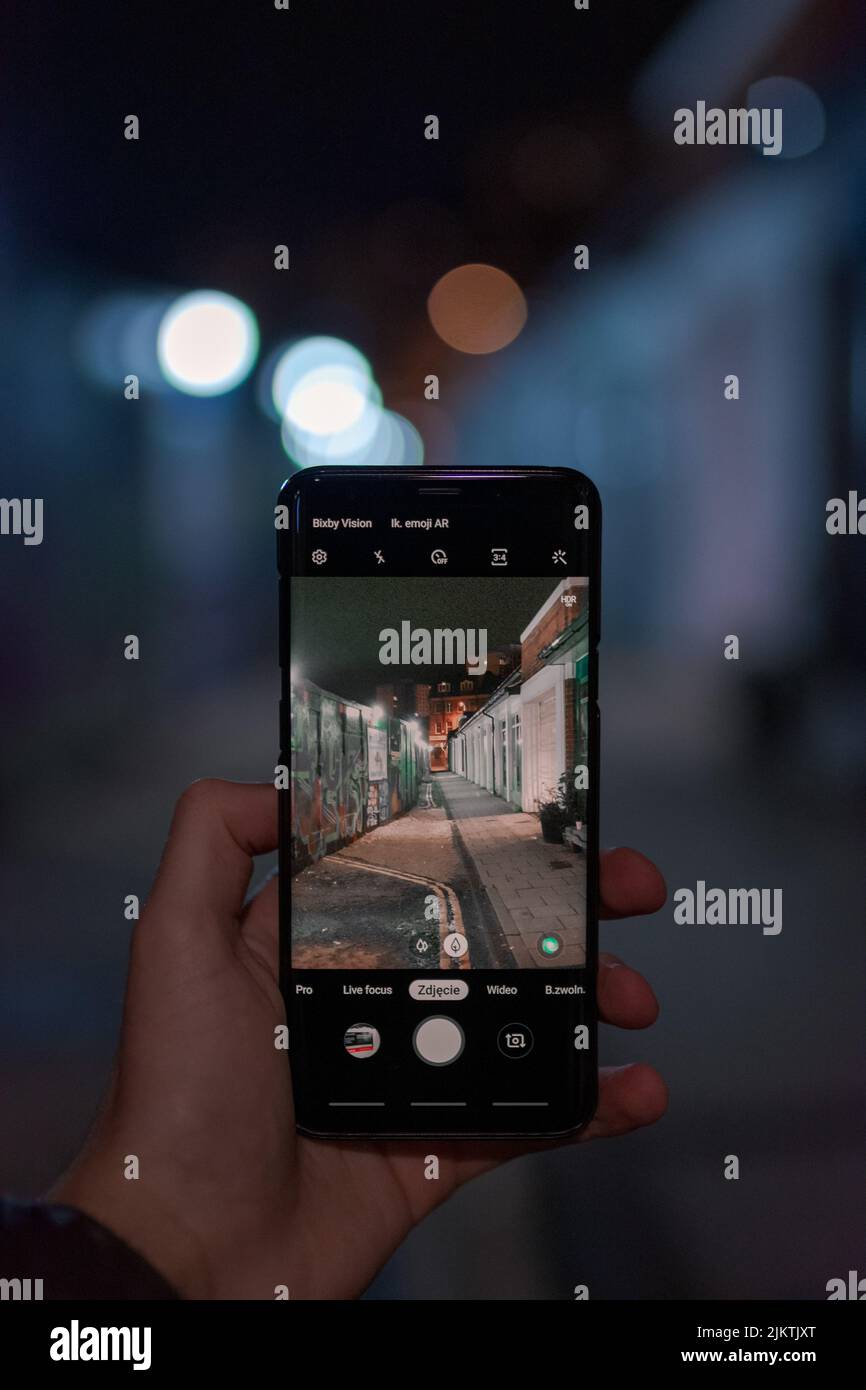 A vertical shot of a hand holding a phone with a turned on camera on a ...