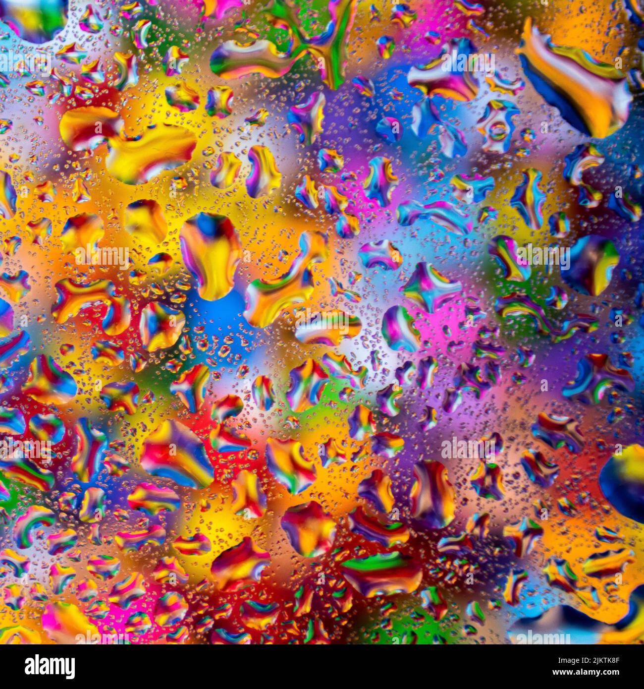 An abstract background of rain droplets on a glass with blurry rainbow ...