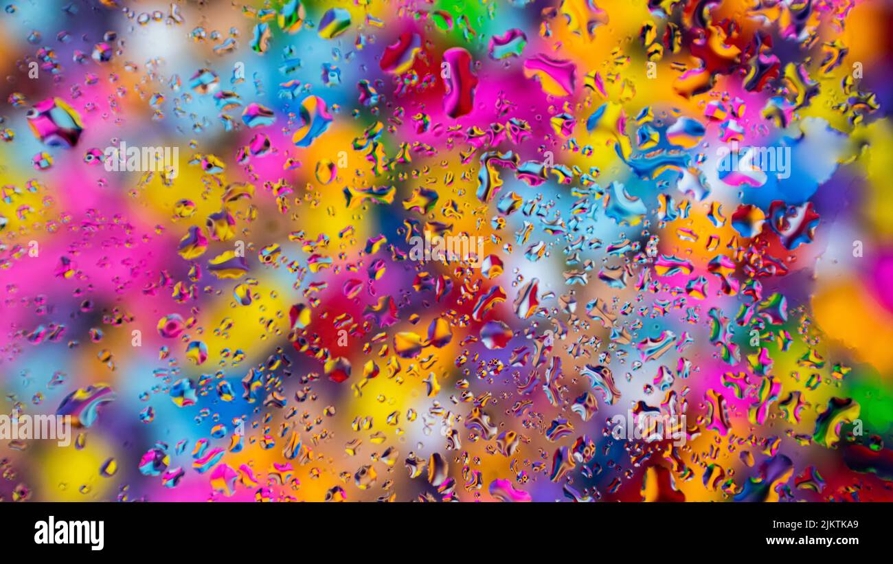 An abstract background of rain droplets on a glass with blurry rainbow ...