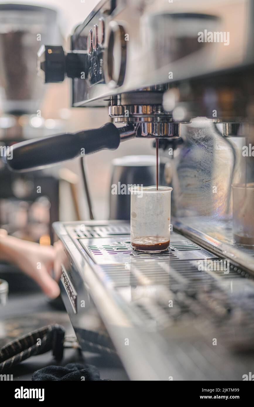 A vertical closeup of a coffee machine pouring espresso into a cup ...