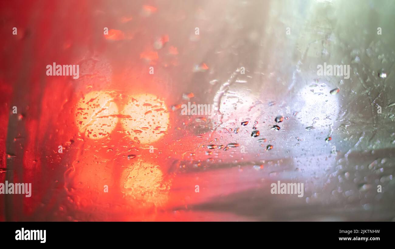 A view of foggy window with rain drops with reflection of car lights ...
