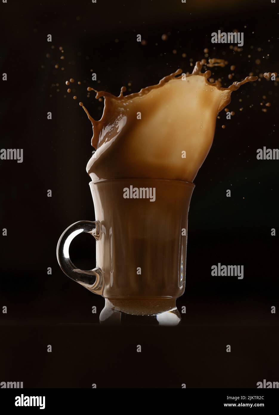 A vertical shot of a glass of karak tea splashed in the air on a black ...