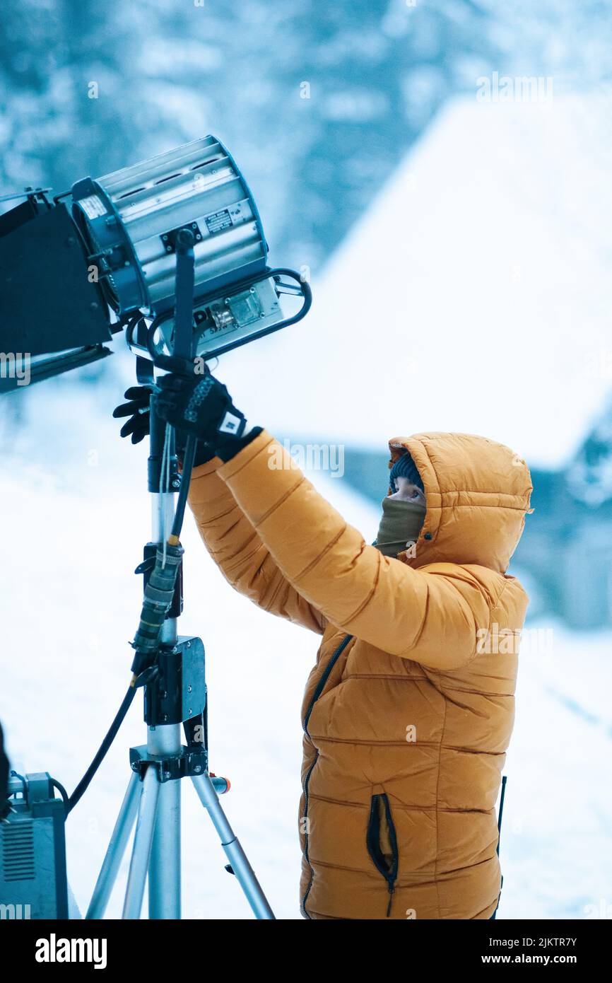 A warmly dresses cameraman adjusting the light equipment in a snowy ...