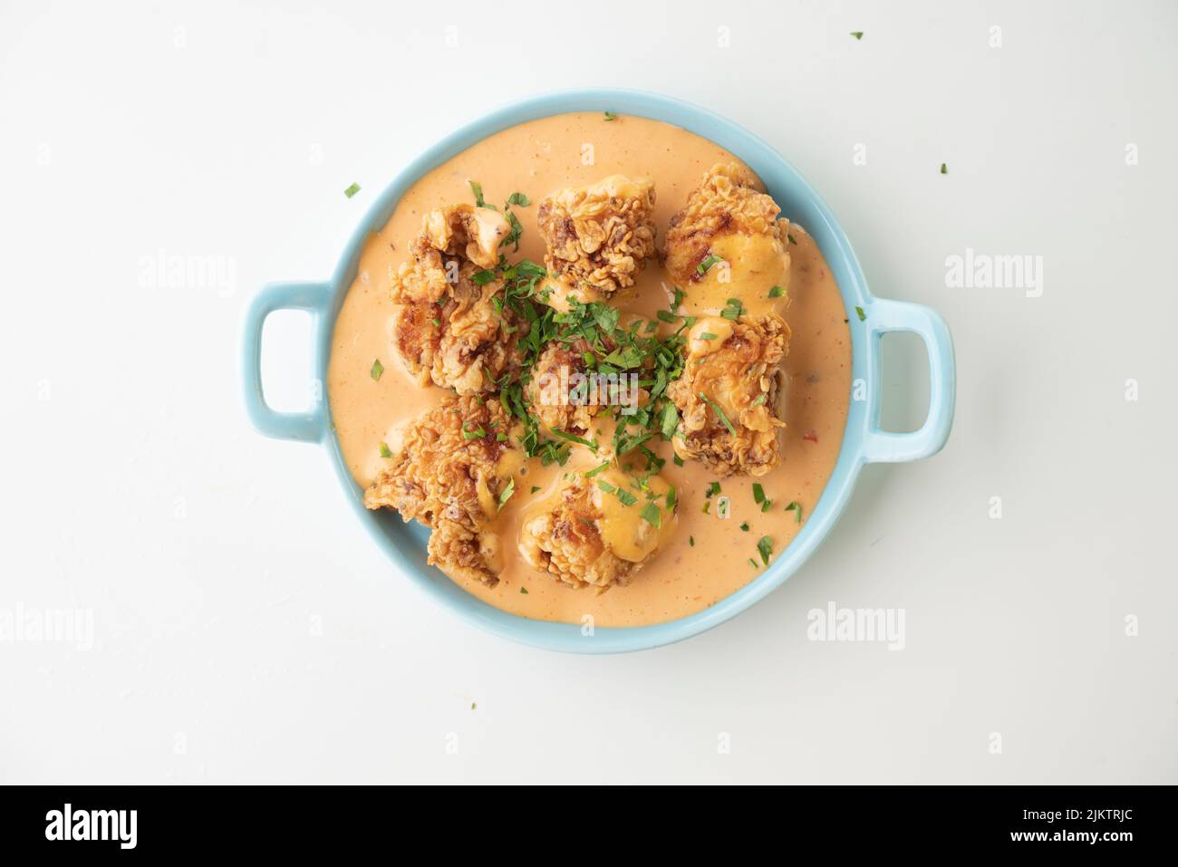 A top view of of fried fish with sauce on it and greens over a white ...