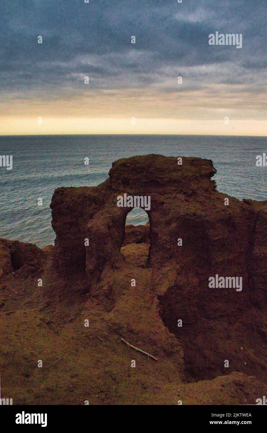 A vertical shot of a rock formation with a hole and the ocean in the ...
