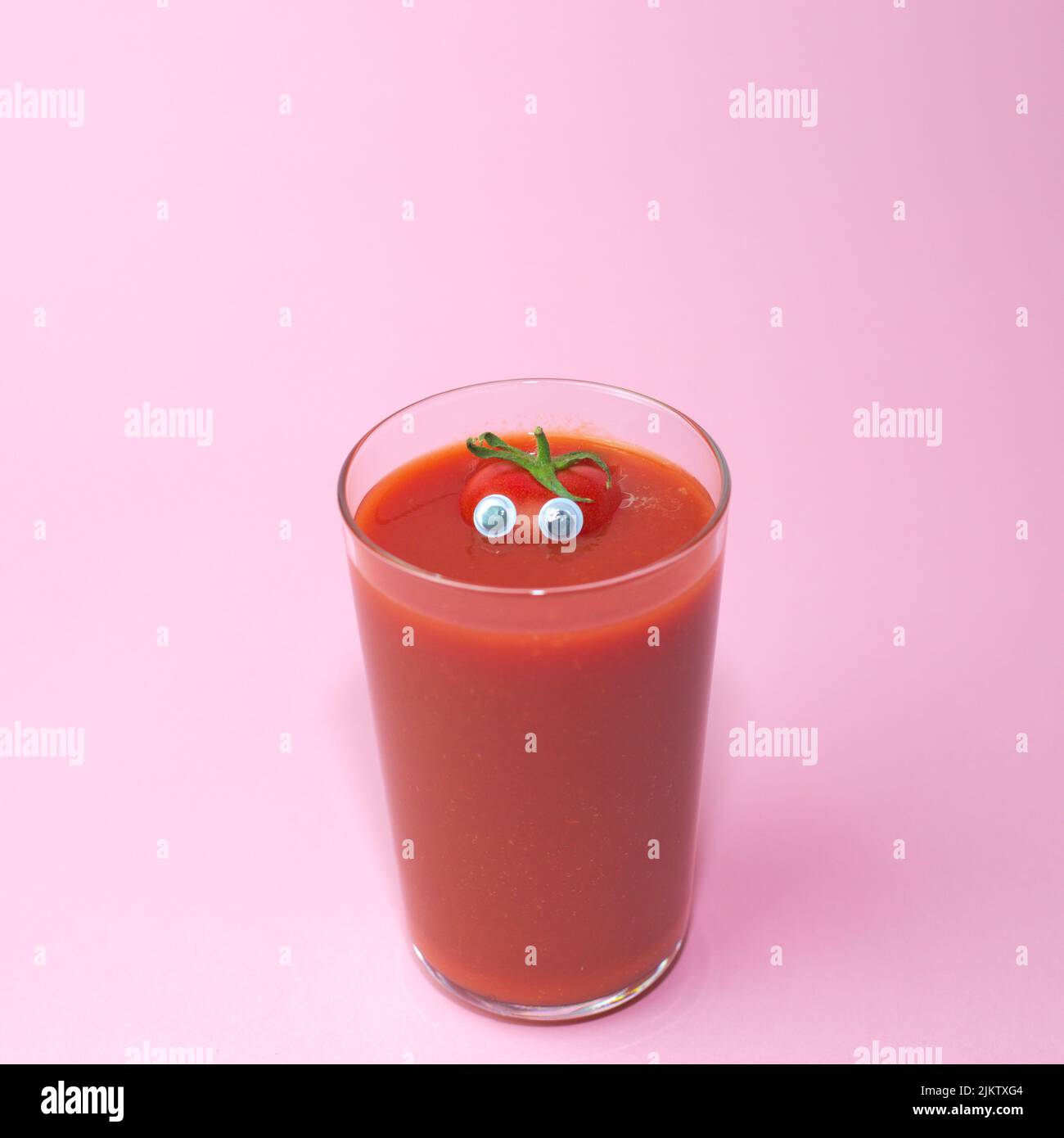 A Glass Of Tomato Juice With A Whole Cherry Tomato With Eyes In It Isolated On A Pink Background