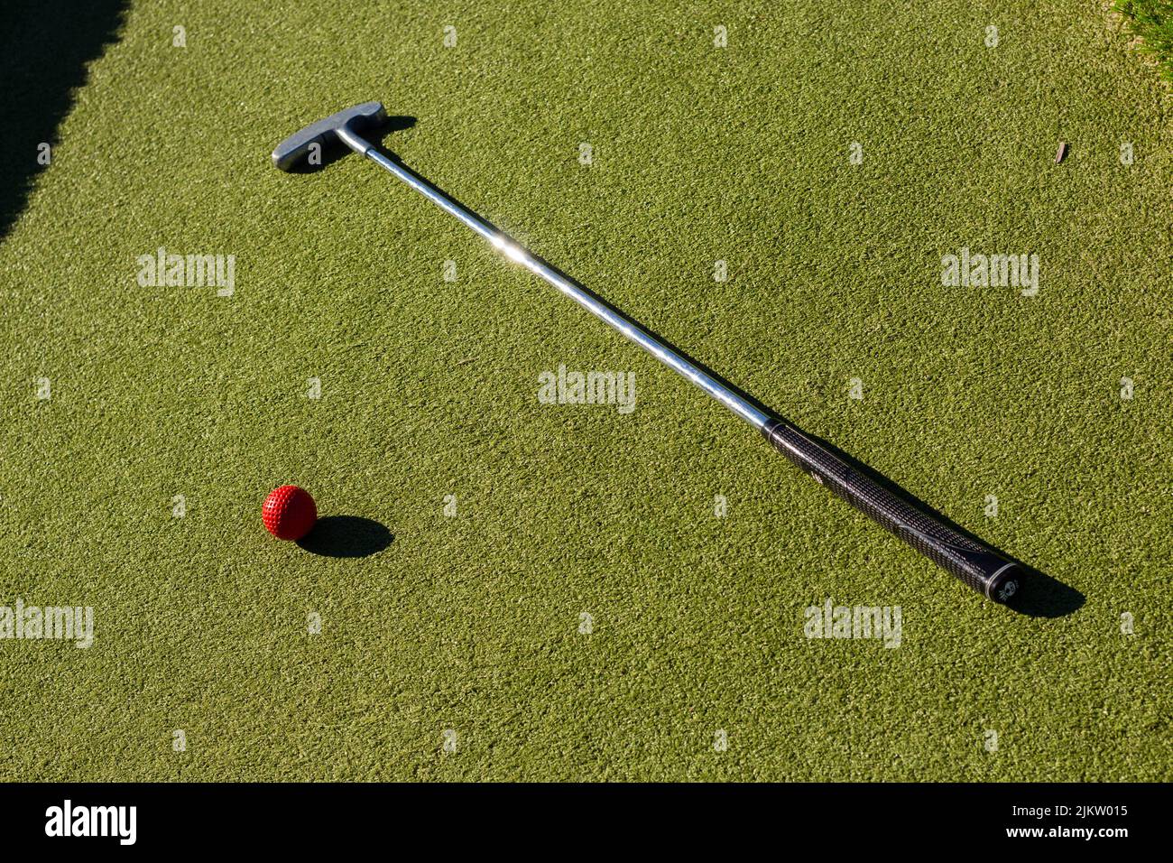 A top view shot of a golf club and a red golf ball on the green grass ...