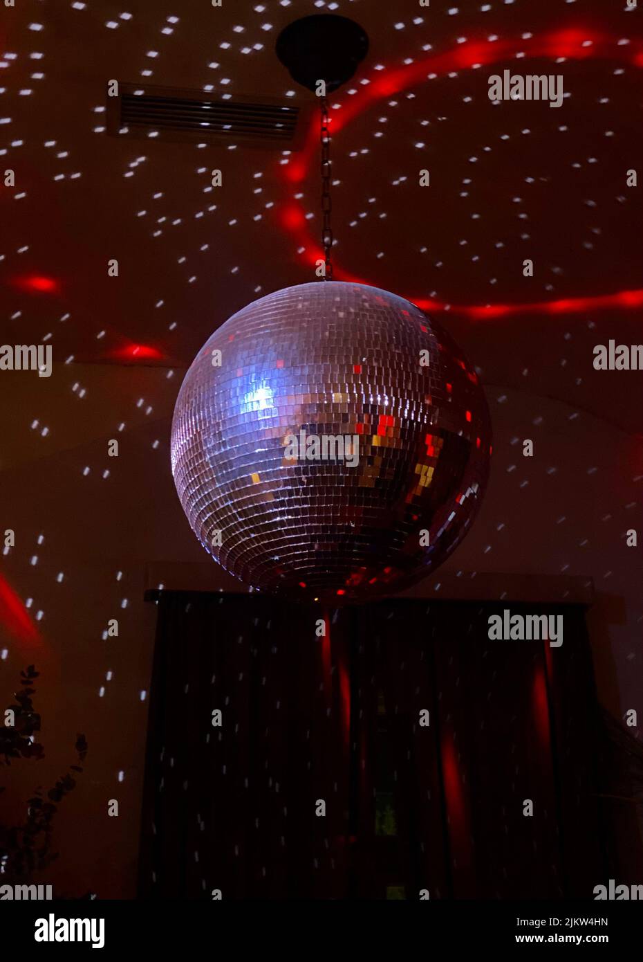 A vertical closeup of the bright disco ball against the dark red ...