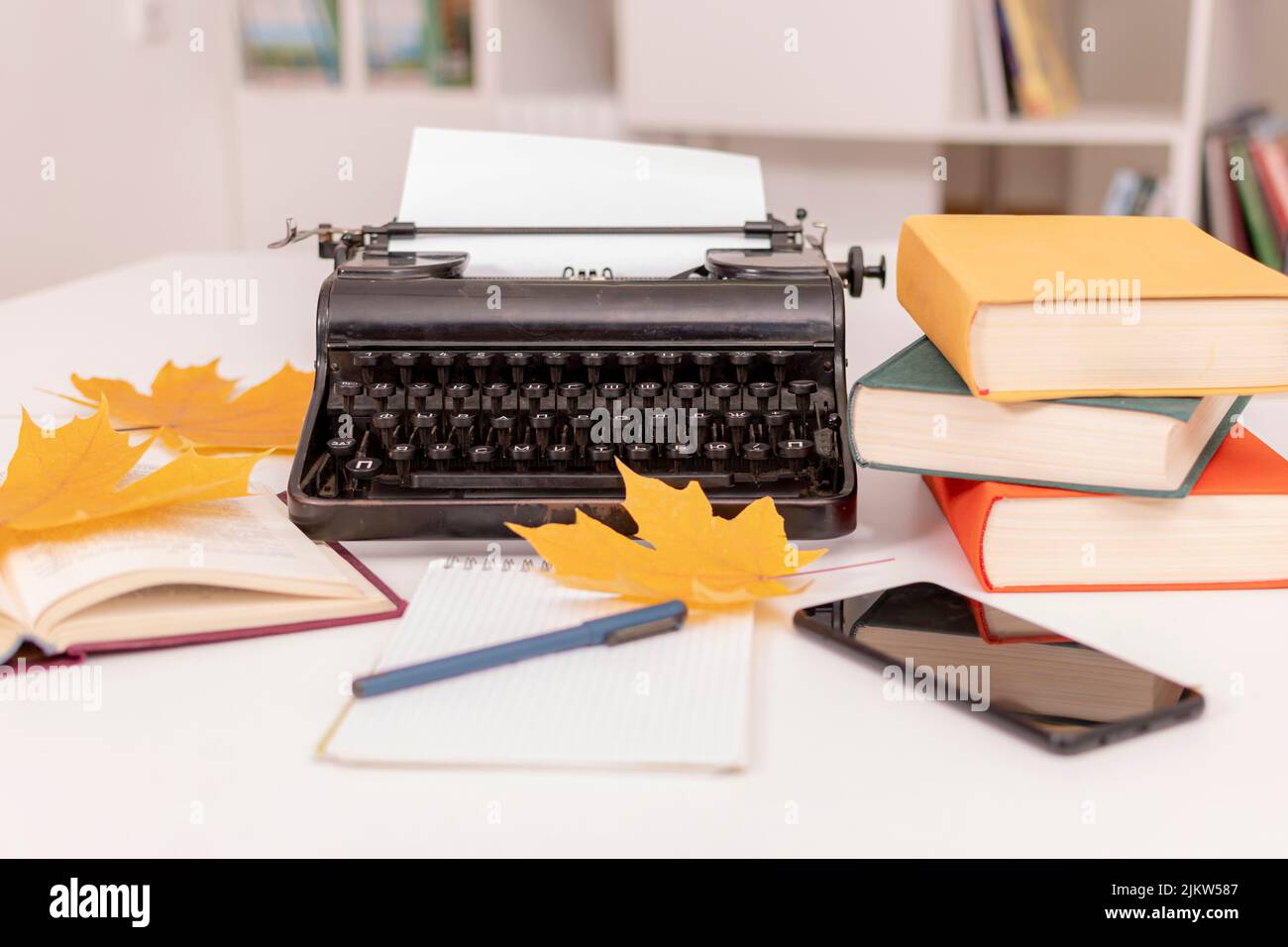 There is retro typewriter on white table. Nearby are books, notebook ...