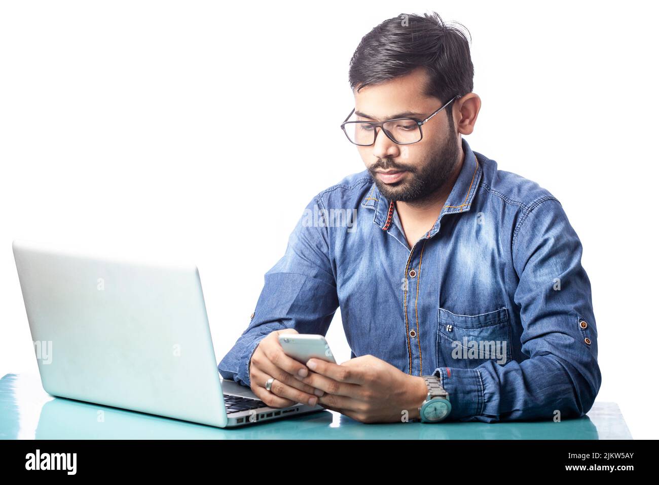 distracted young man typing on cell phone in front of a laptop in white ...