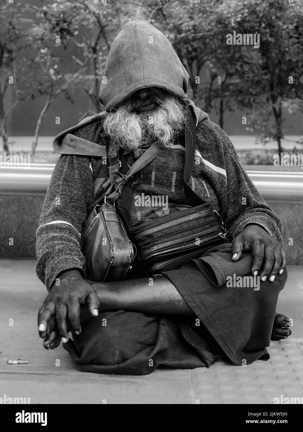 A vertical grayscale shot of a homeless Tamil Indian male sitting on ...