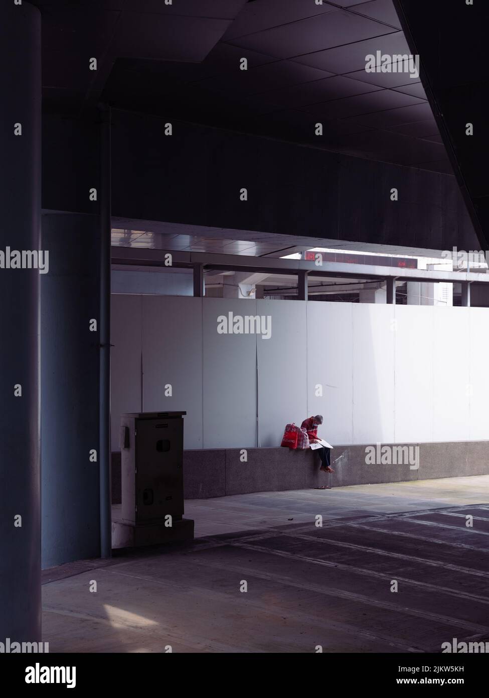 A vertical distant view of a male waiting for a bus at the MRT station ...