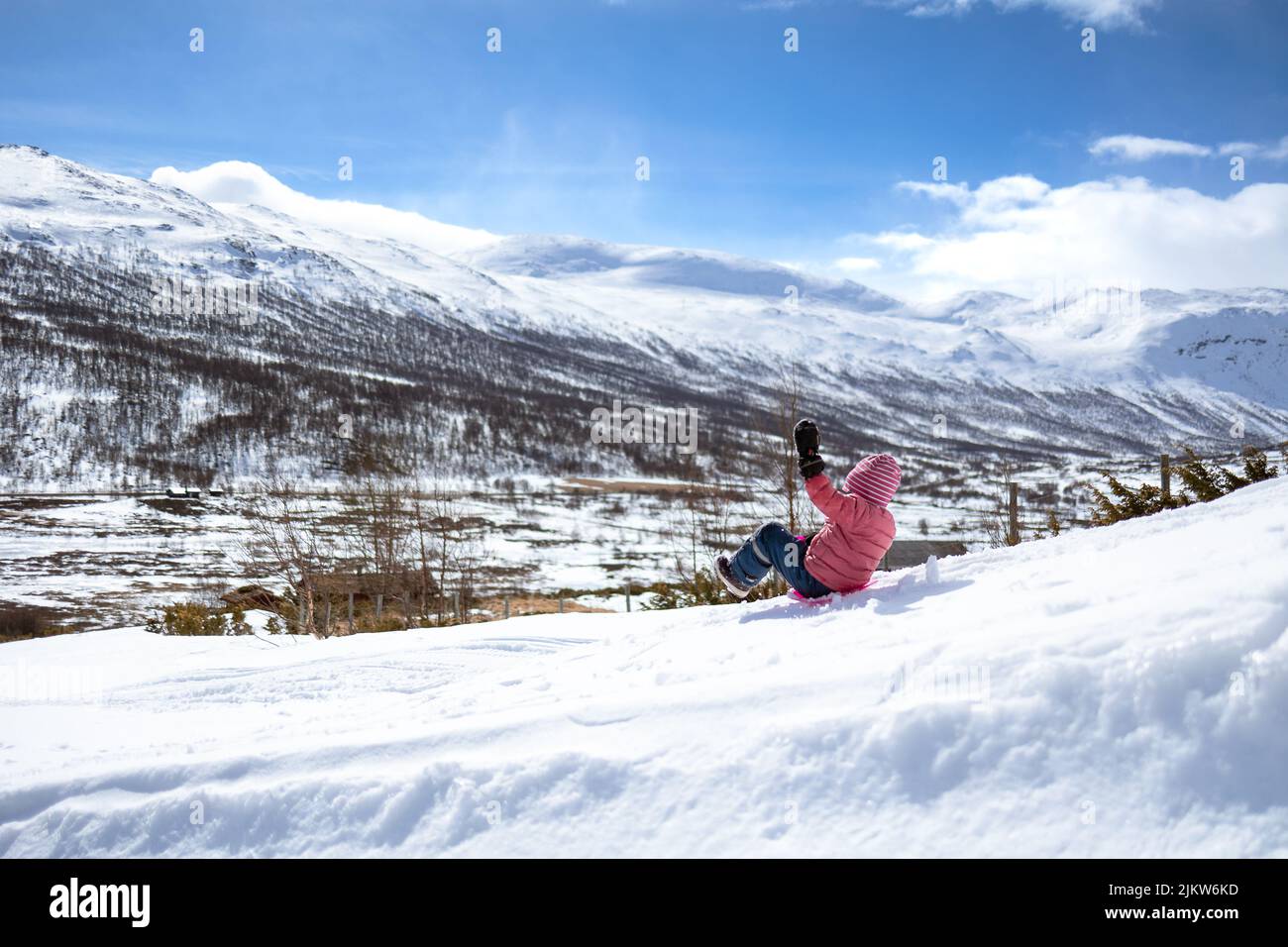 The little girl is sliding on the snow against the background of ...