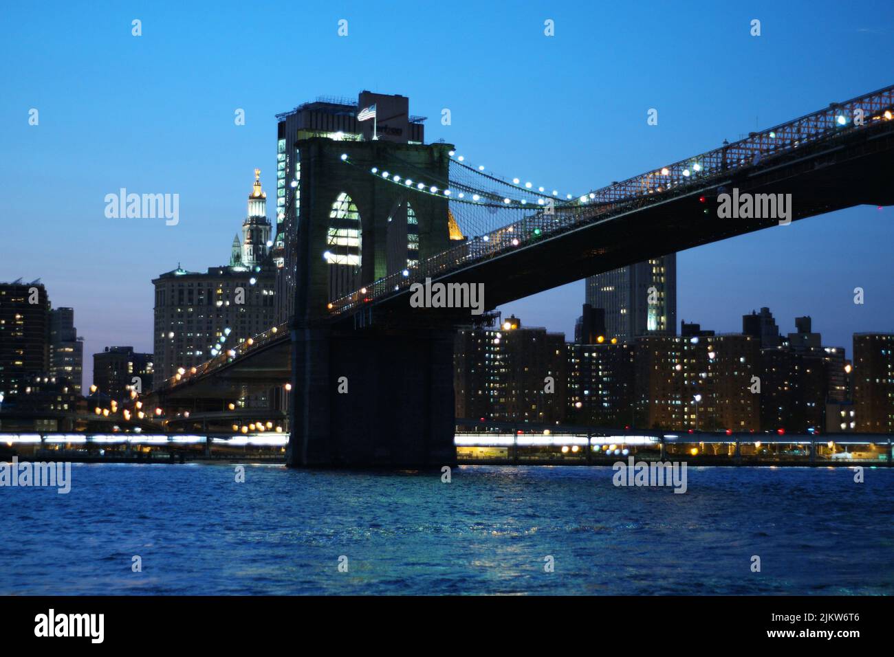 The famous Brooklyn Bridge and the NYC skyline behind with lights on in ...
