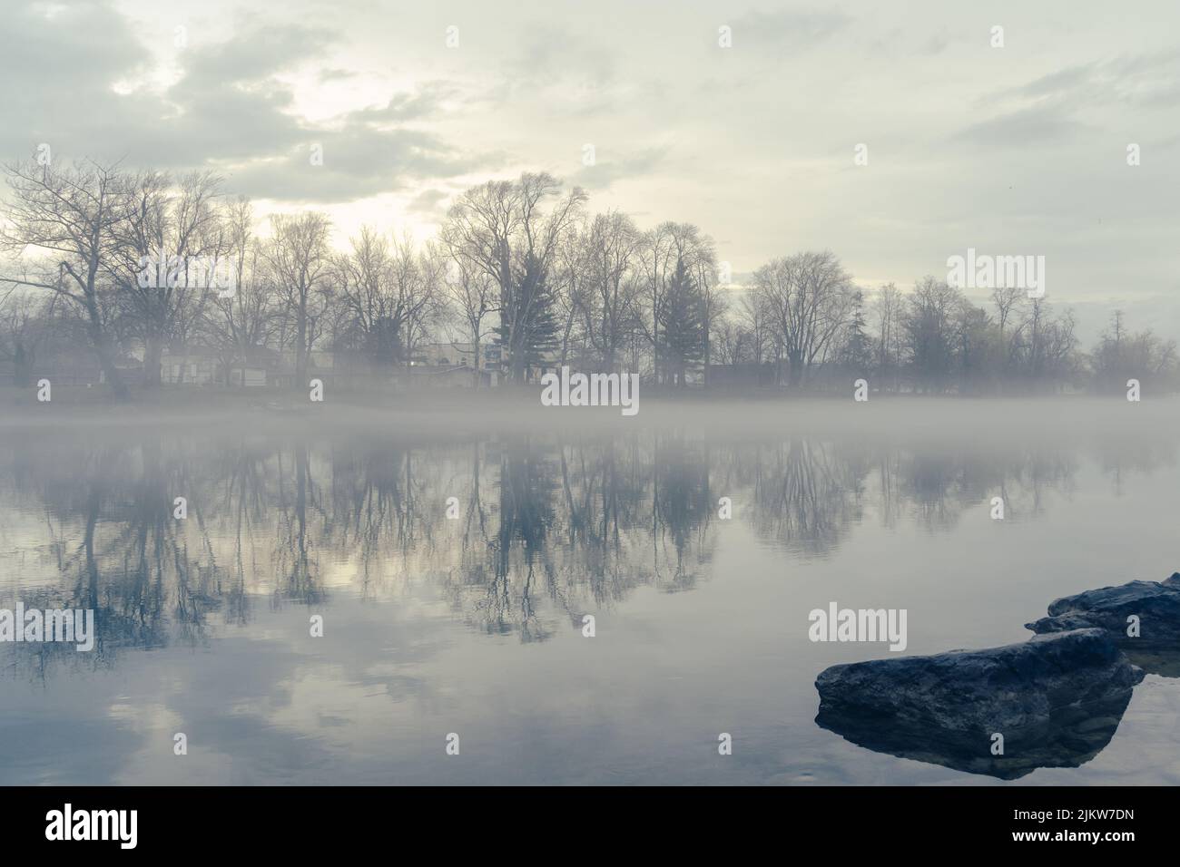 A beautiful view of a reflective lake with trees on a foggy day Stock ...