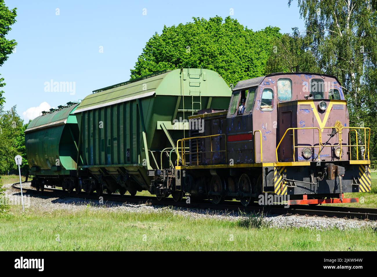 A small brown shunting diesel locomotive pulls two green bulk wagons ...