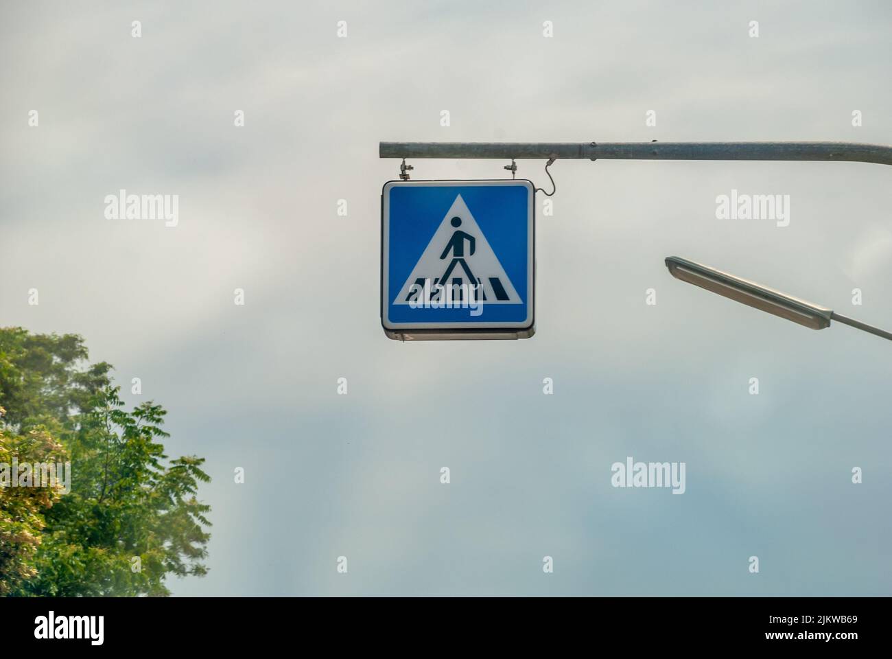 A blue pedestrian crossing sign hanging on a steel pole in the street ...