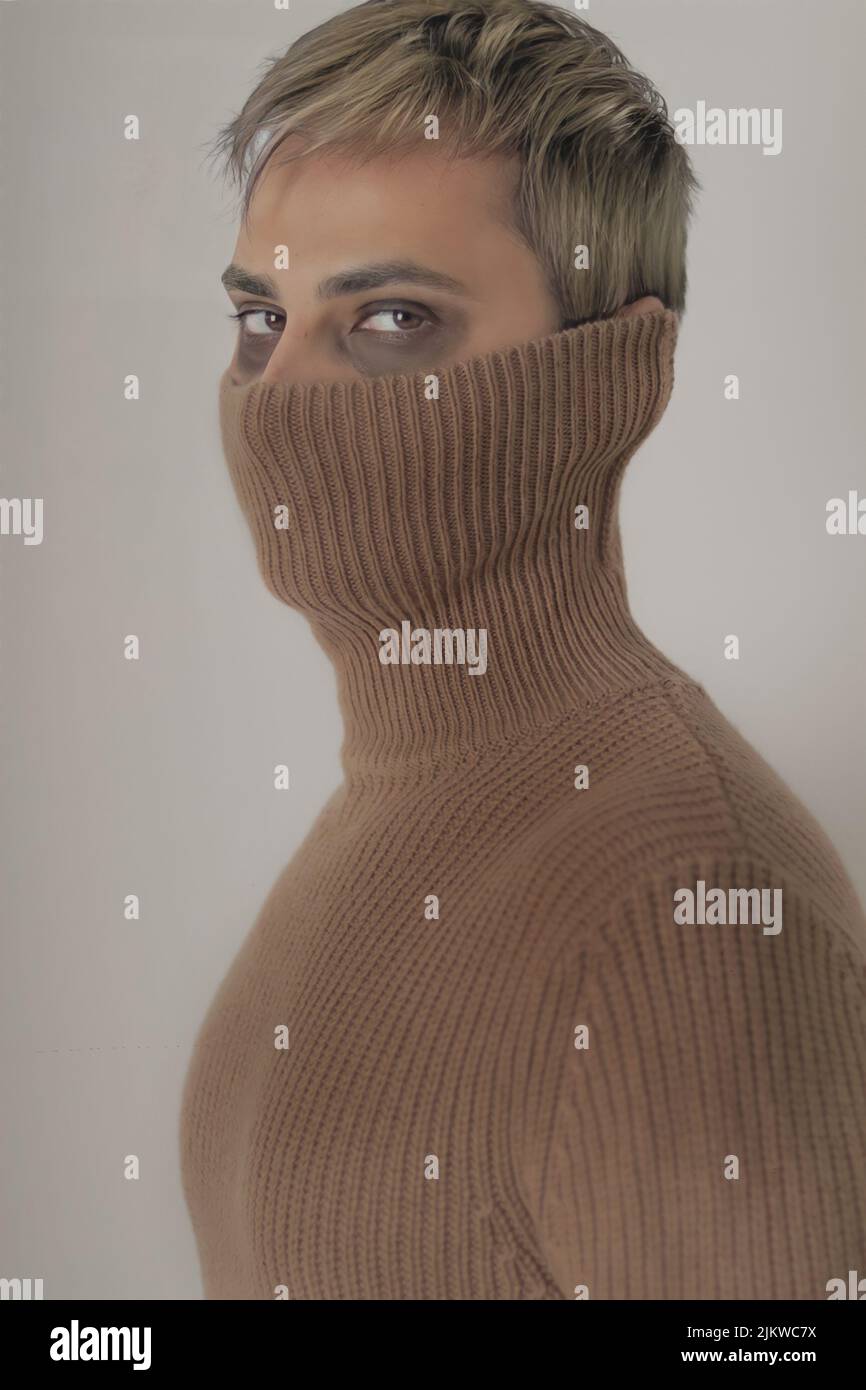 A vertical closeup of a male covering his face with a brown turtleneck ...