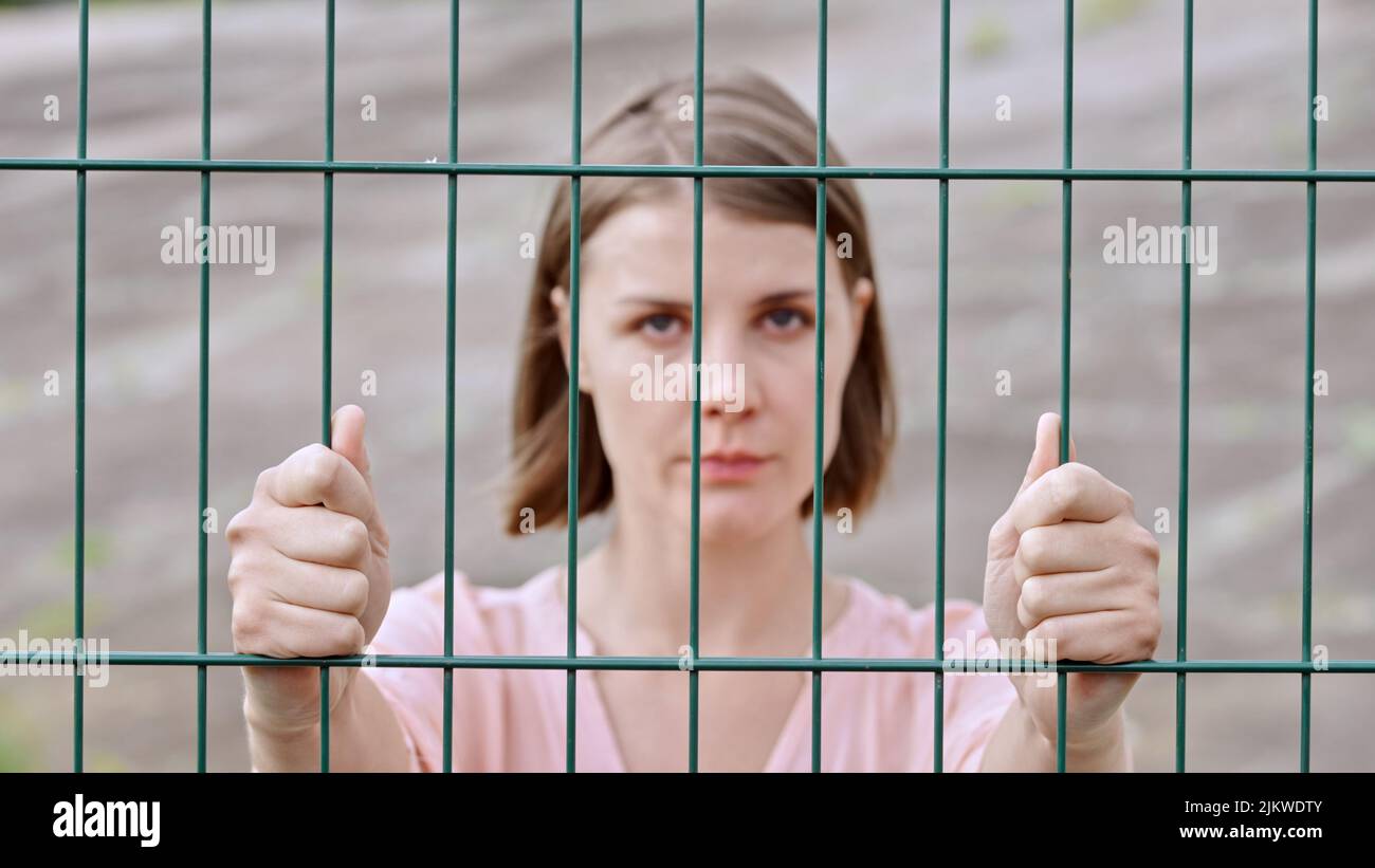 Caucasian young woman with short hair standing behind a fence, looking ...