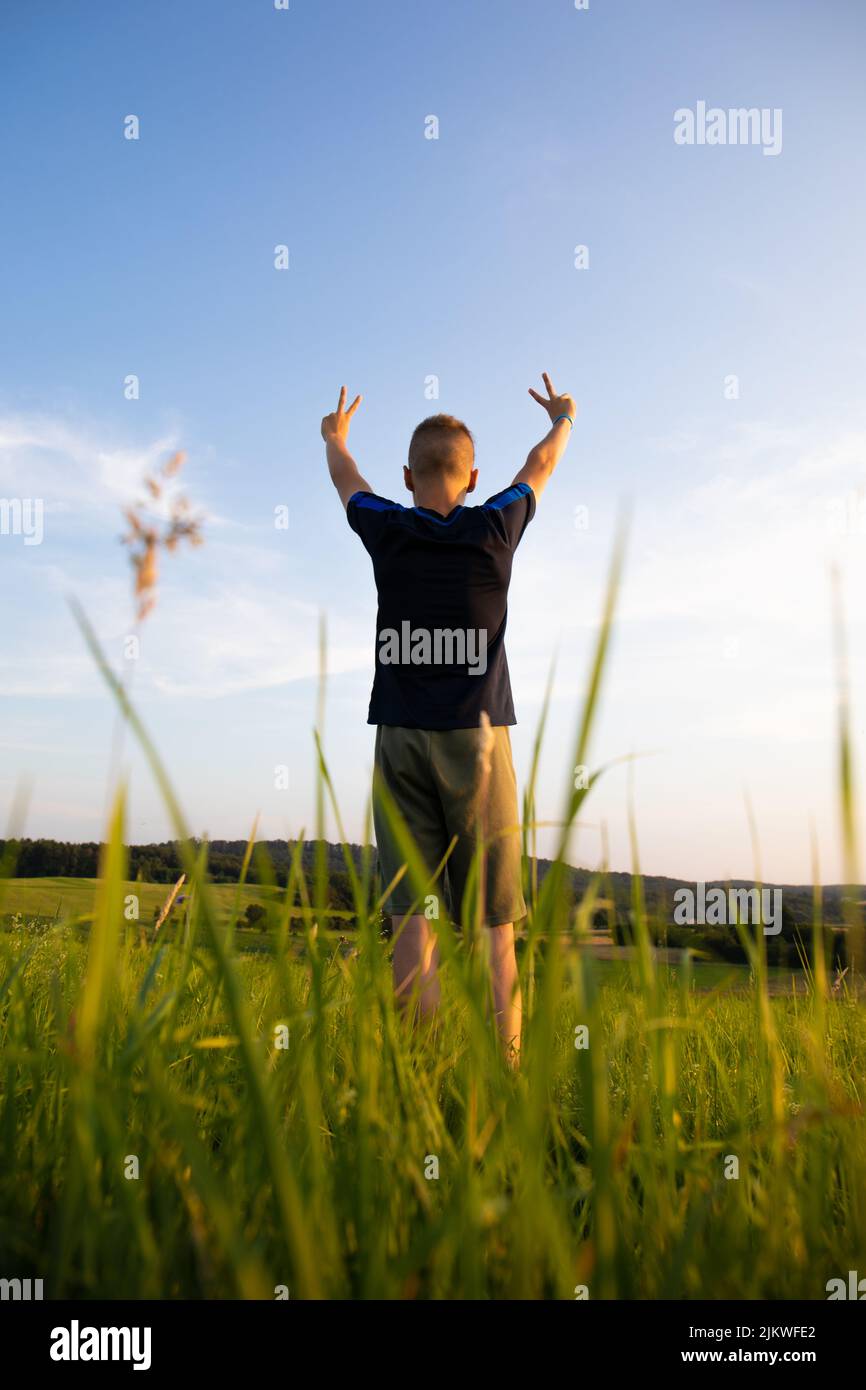 A vertical rear view of a young boy showing victory sign with his ...