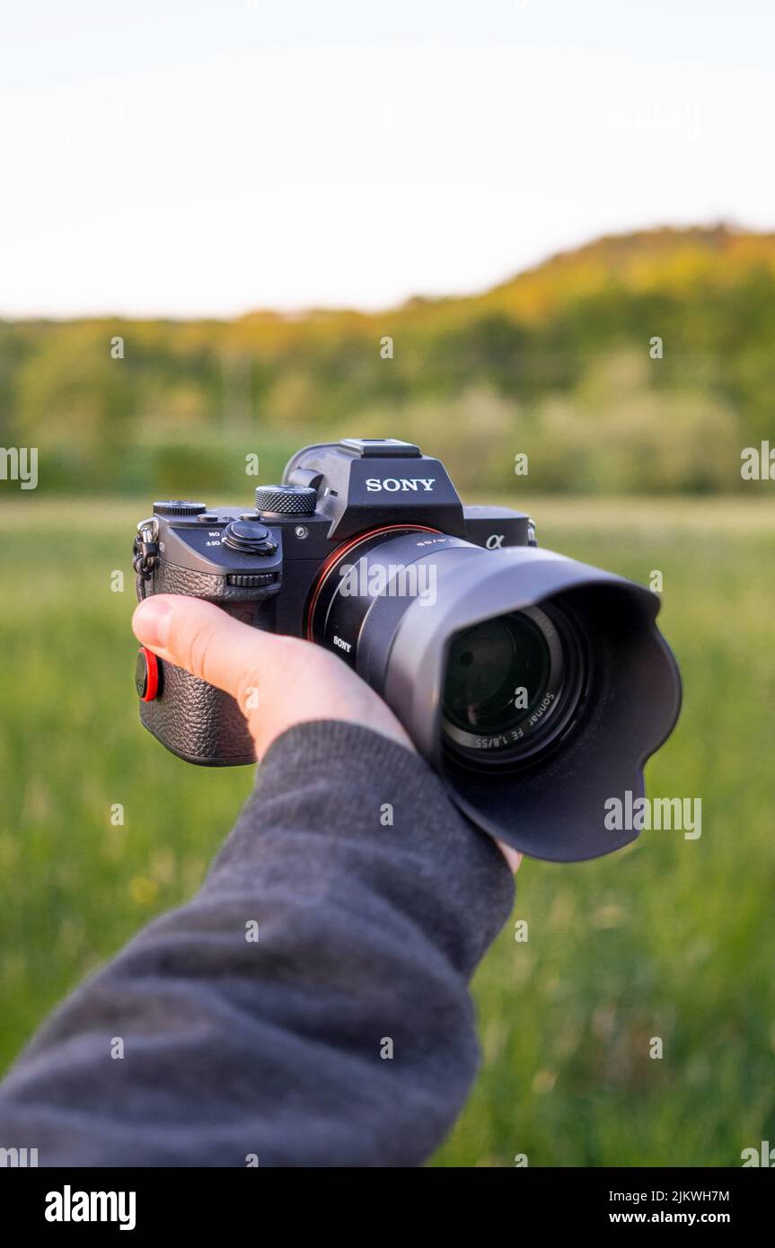 A vertical shot of a hand holding a Sony camera with a field background ...