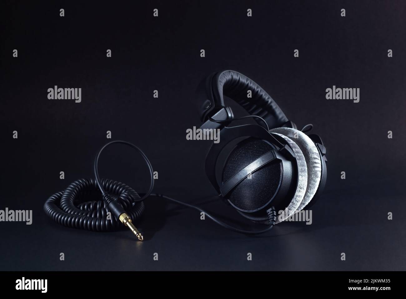 Closed-back studio headphones with a coiled cable stand sideways on a ...