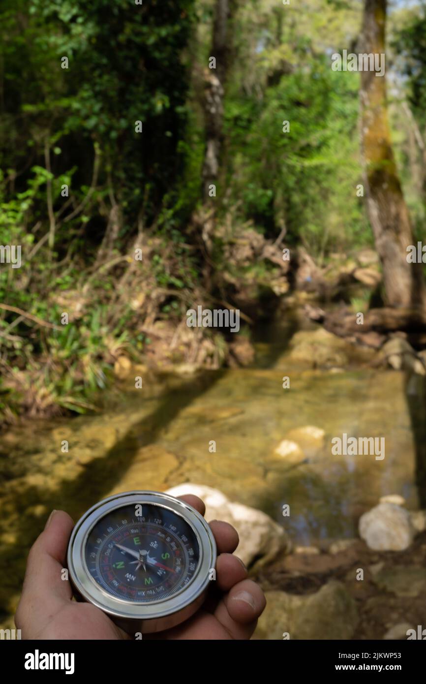 man's hand holding a compass in the forest with a mountain river in the ...