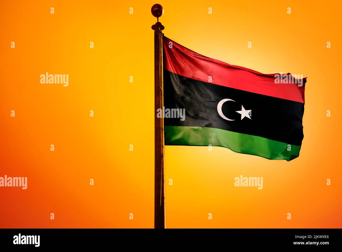 The national flag of Libya on a flagpole isolated on an orange ...