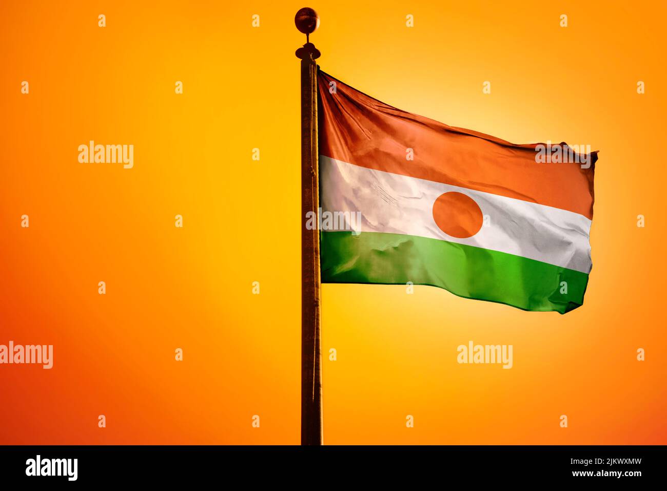 The national flag of Niger on a flagpole isolated on an orange ...