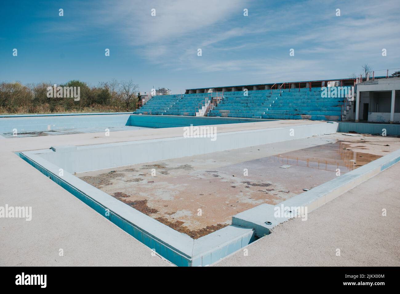 A swimming pool without water and dirty amid green trees on a sunny day ...