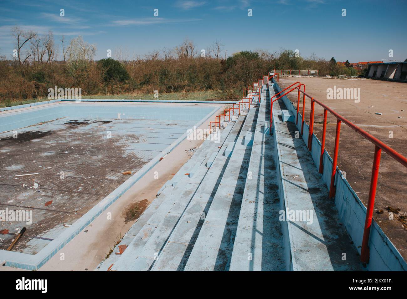A swimming pool without water and dirty amid green trees on a sunny day ...