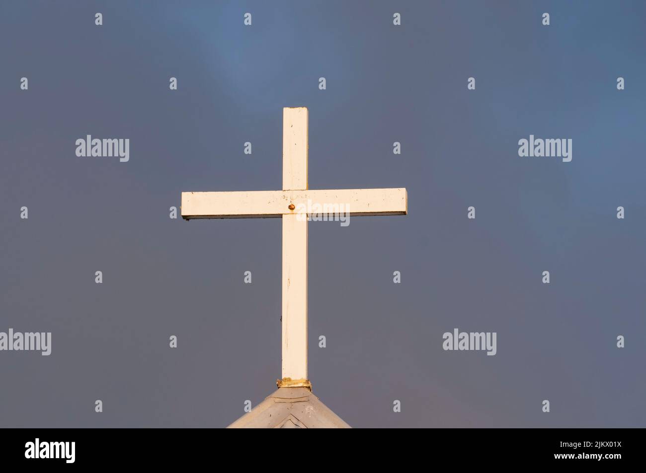 A simple white wooden cross on a church lit by Late afternoon sun ...