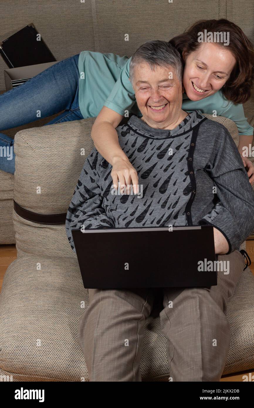 Smiling two woman looking at laptop screen, checking finances, sitting ...