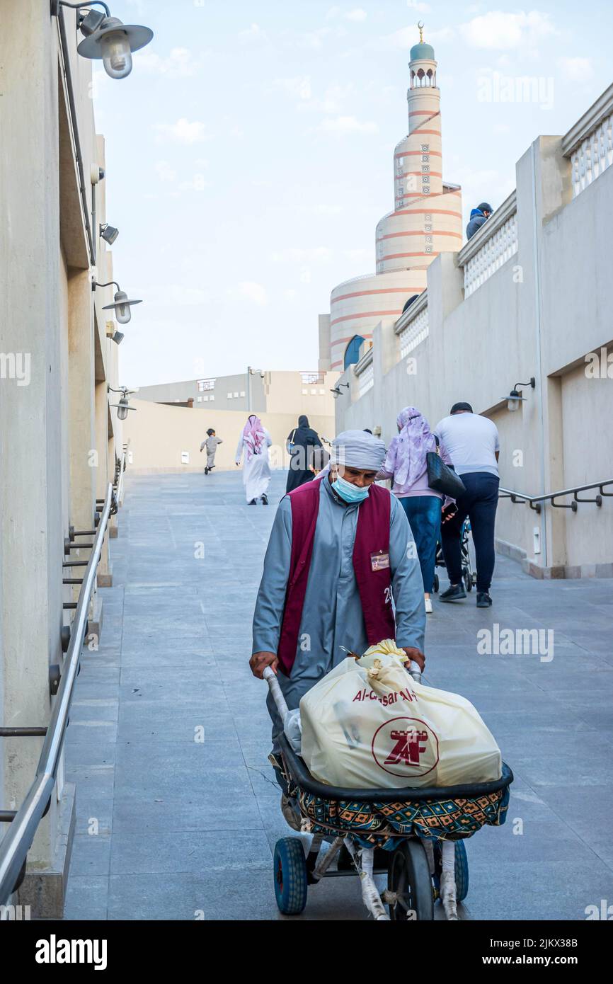 Vertical shot of a worker pushing a trolley and people in Souq Waqif, a ...
