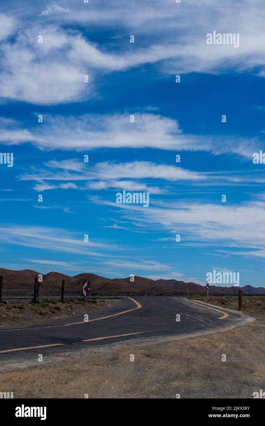 A vertical shot of a curvy road in the countryside under the blue clear ...