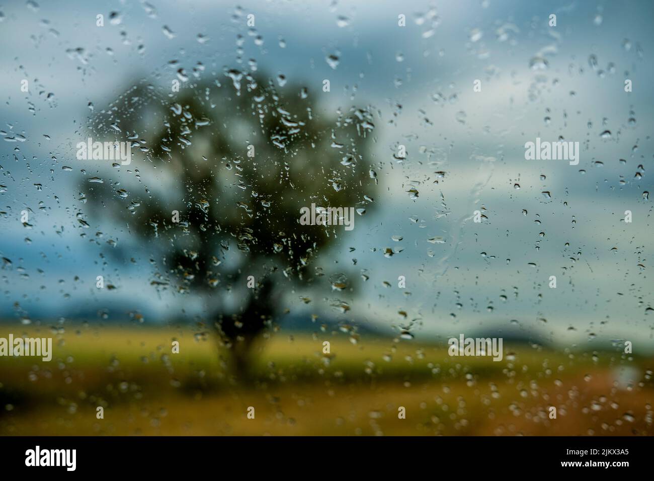 A shallow focus shot of the window with rain drops against the blurry ...