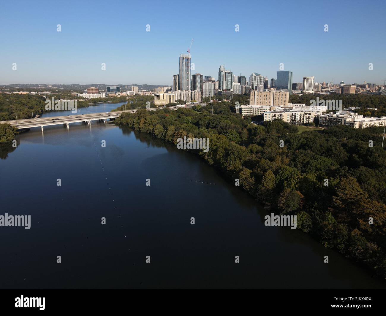 A bird's eye view of a river reflecting green trees and a brigde ...